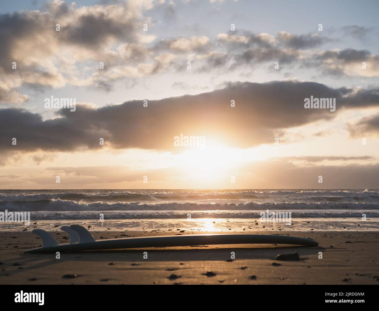 A surfboard lying on the beach shore and sunrise over the ocean waves ...