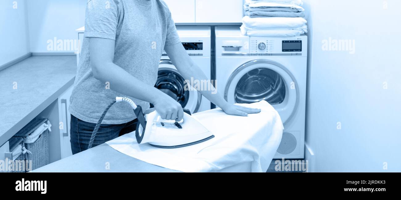 ironing white shirt on board in laundry room with washing machine on ...