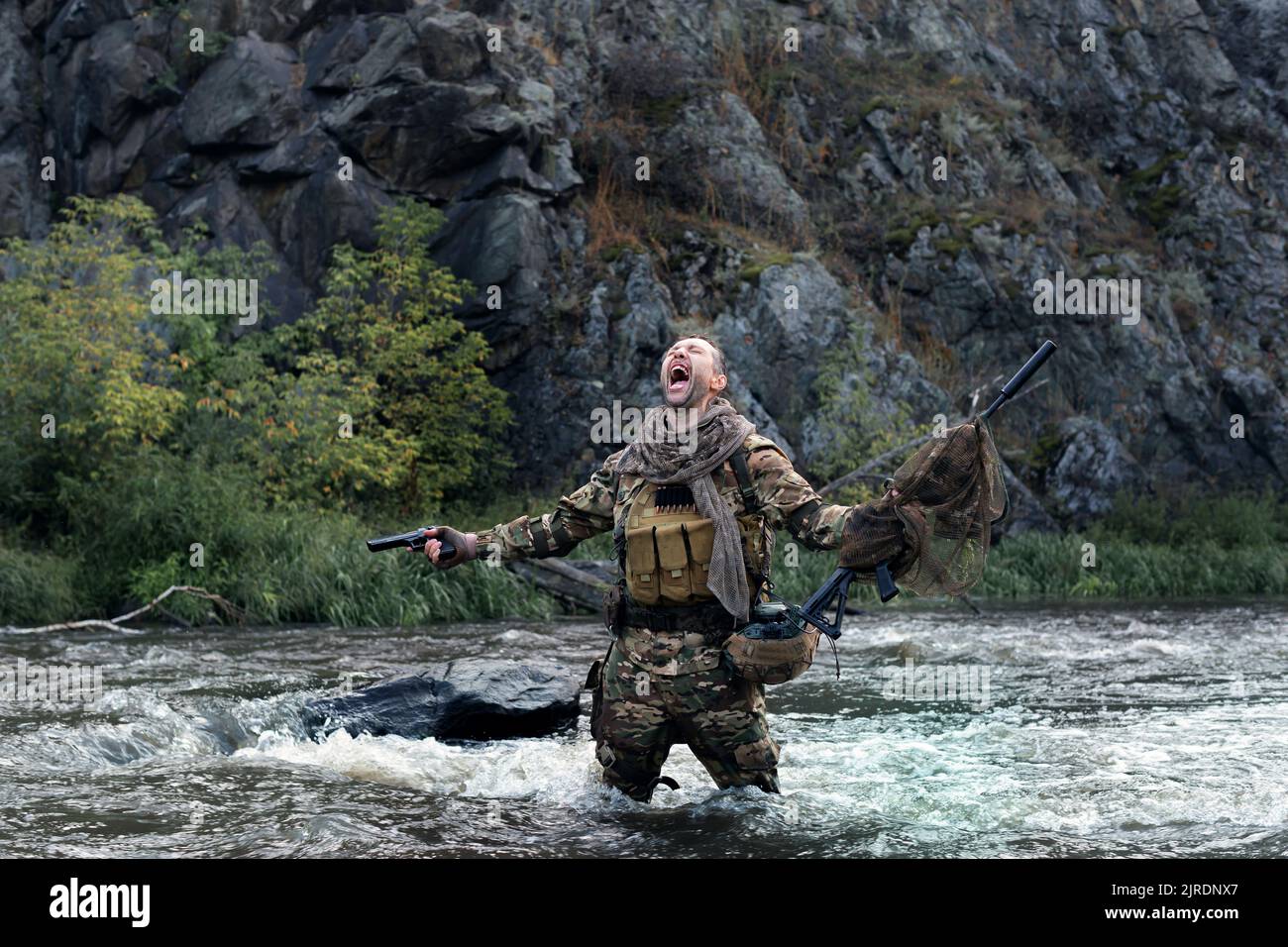 Lone mercenary soldier stands knee-deep in river and screaming, arms ...