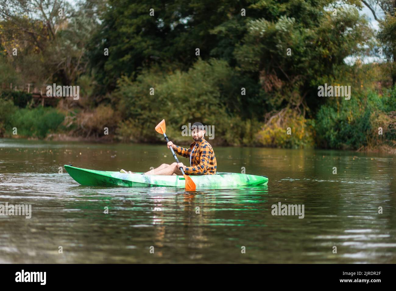 Pretty bearded caucasian man in shirt and cap kayaking at the river ...