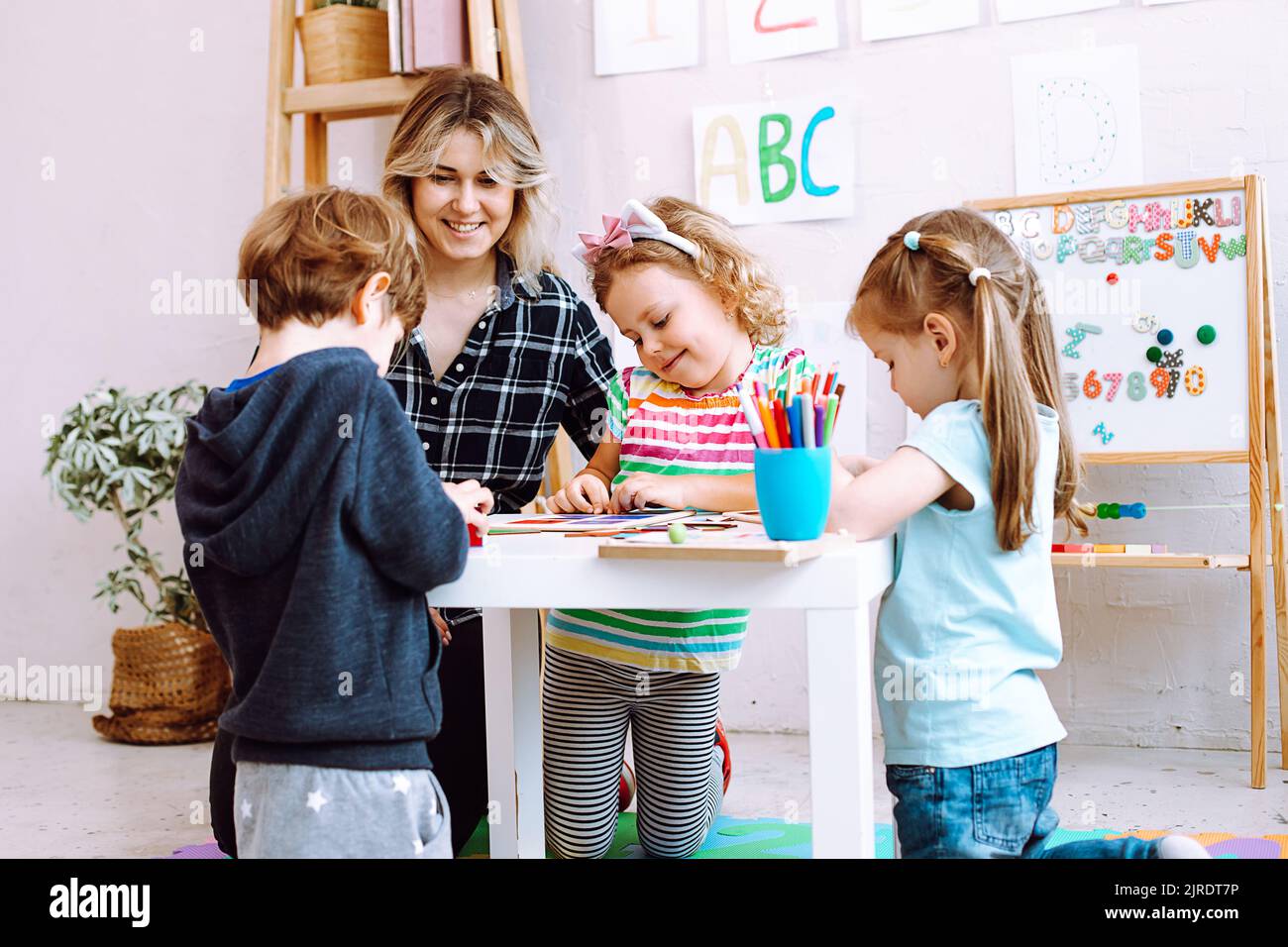 Portrait of young woman sitting at table around children playing ...