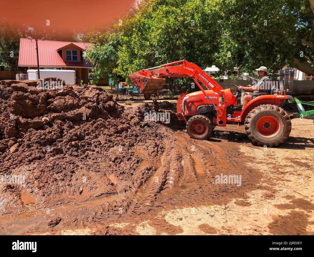 A volunteer on a small tractor scrapes up mud from a parking lot and ...