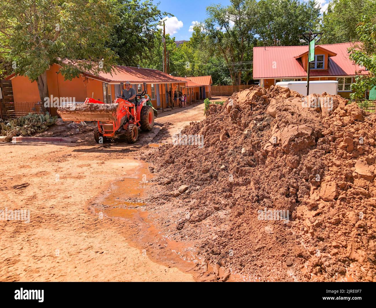 A volunteer on a small tractor scrapes up mud from a parking lot and ...
