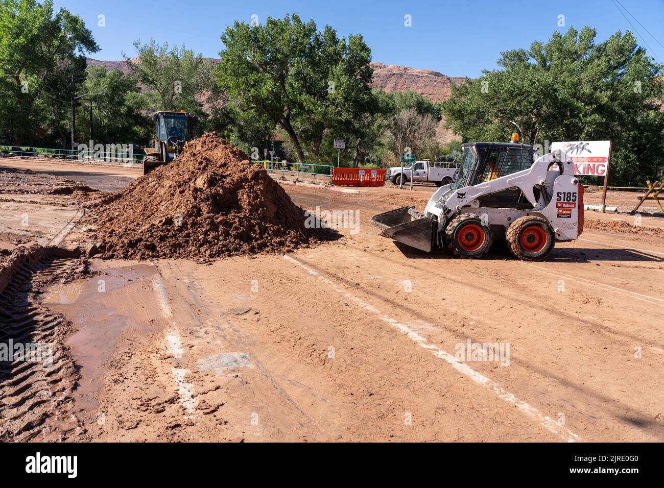 A skid steer loader scrapes up mud off the street the day after a flash ...