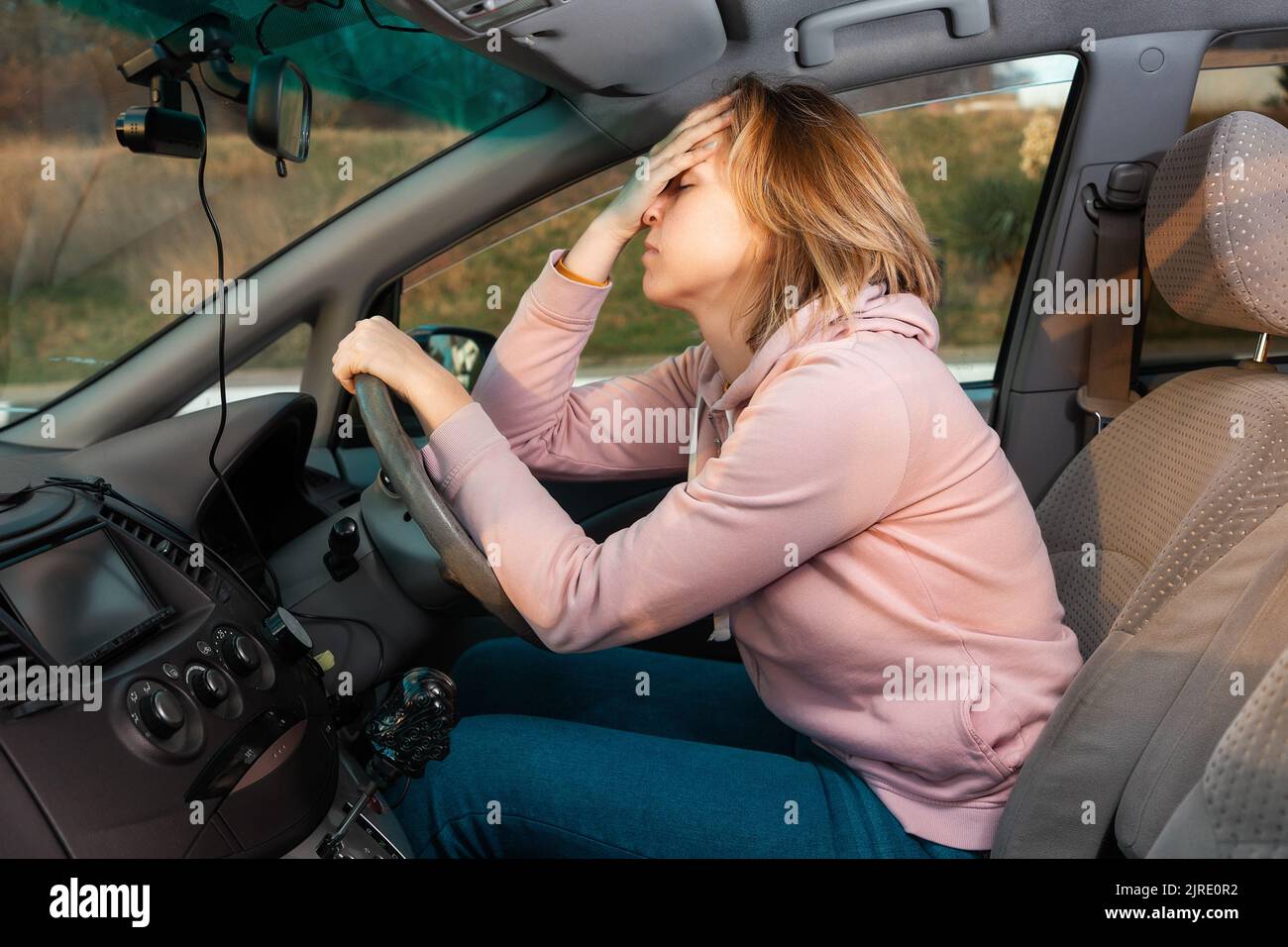 Portrait of a young blonde stressed woman is sitting behind the wheel ...