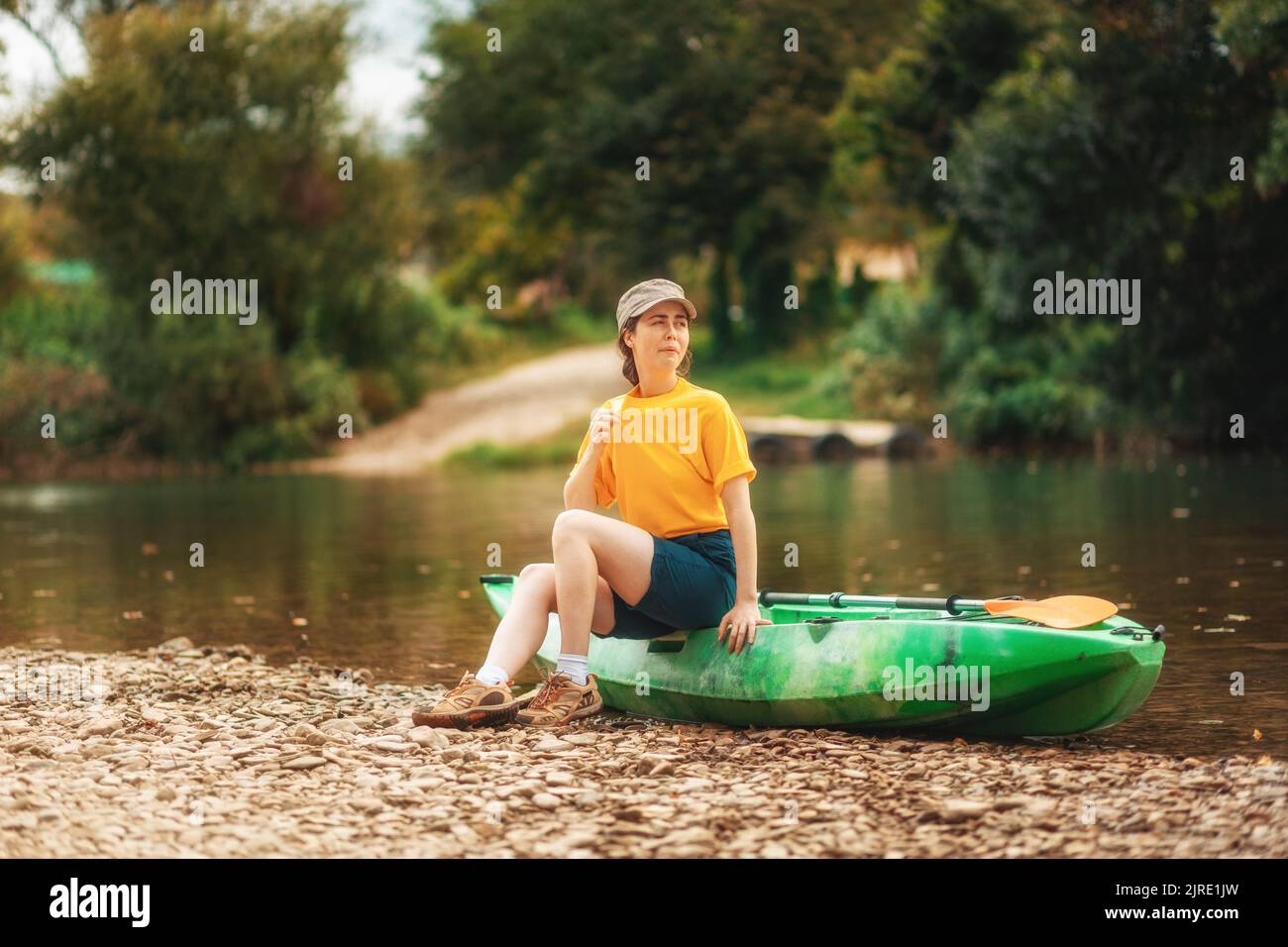 Summer vacation in the park. A woman is sitting on a kayak, fanning ...