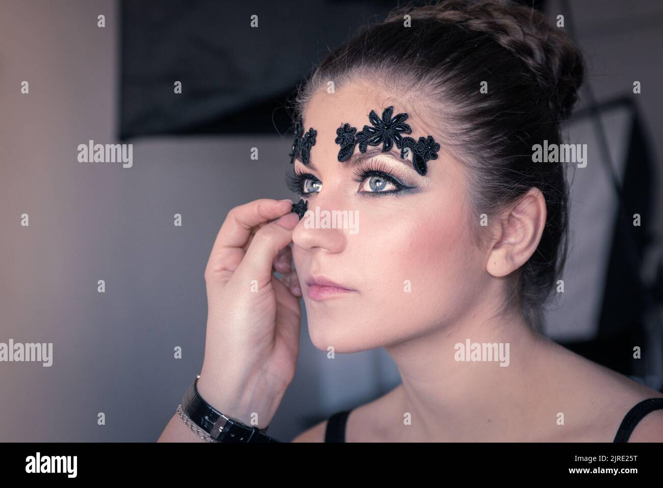 The make-up artist is applying a decorative black lace band on young ...