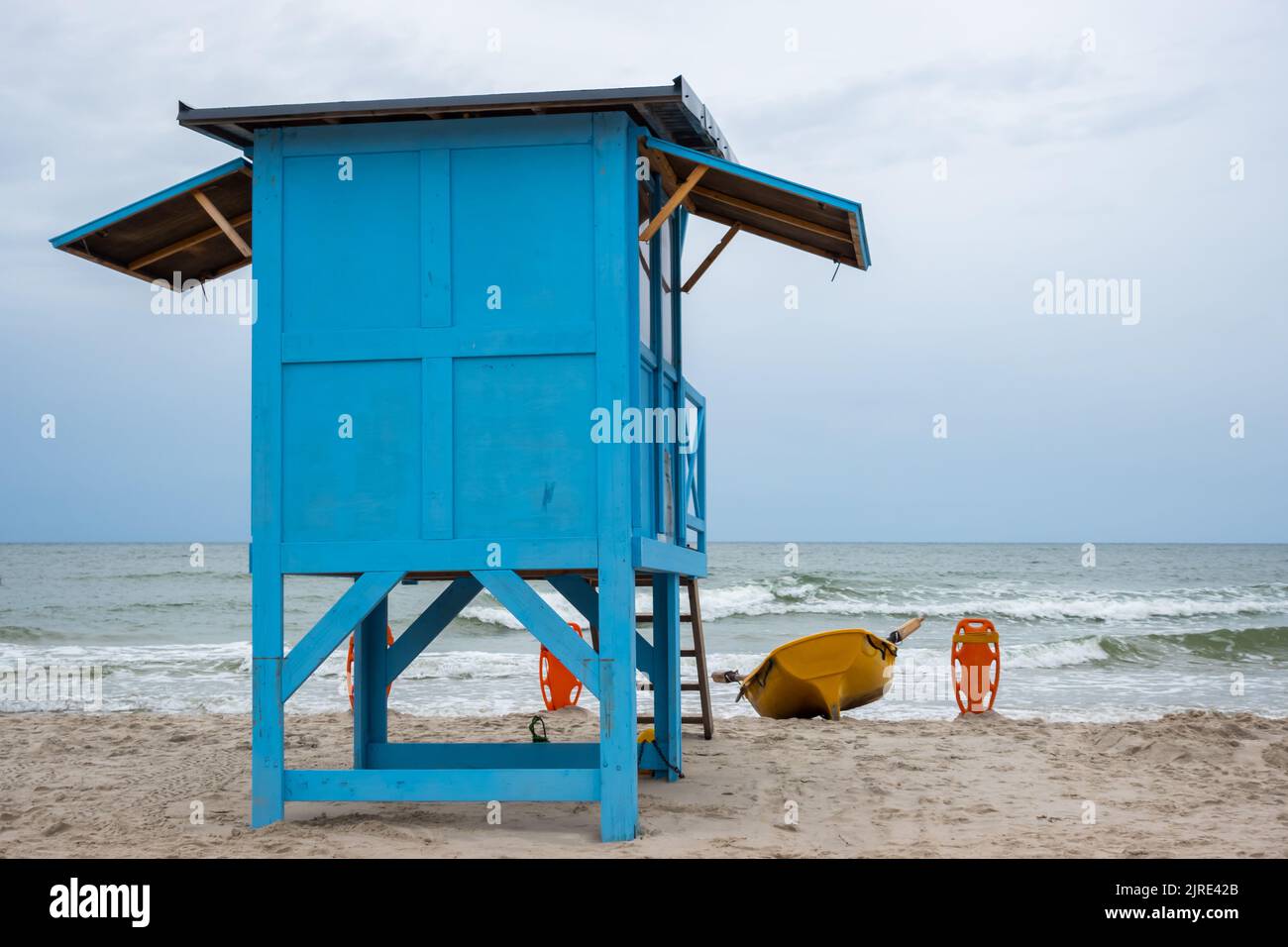 A blue lifeguard booth on the beach on a cloudy day. A yellow lifeboat ...