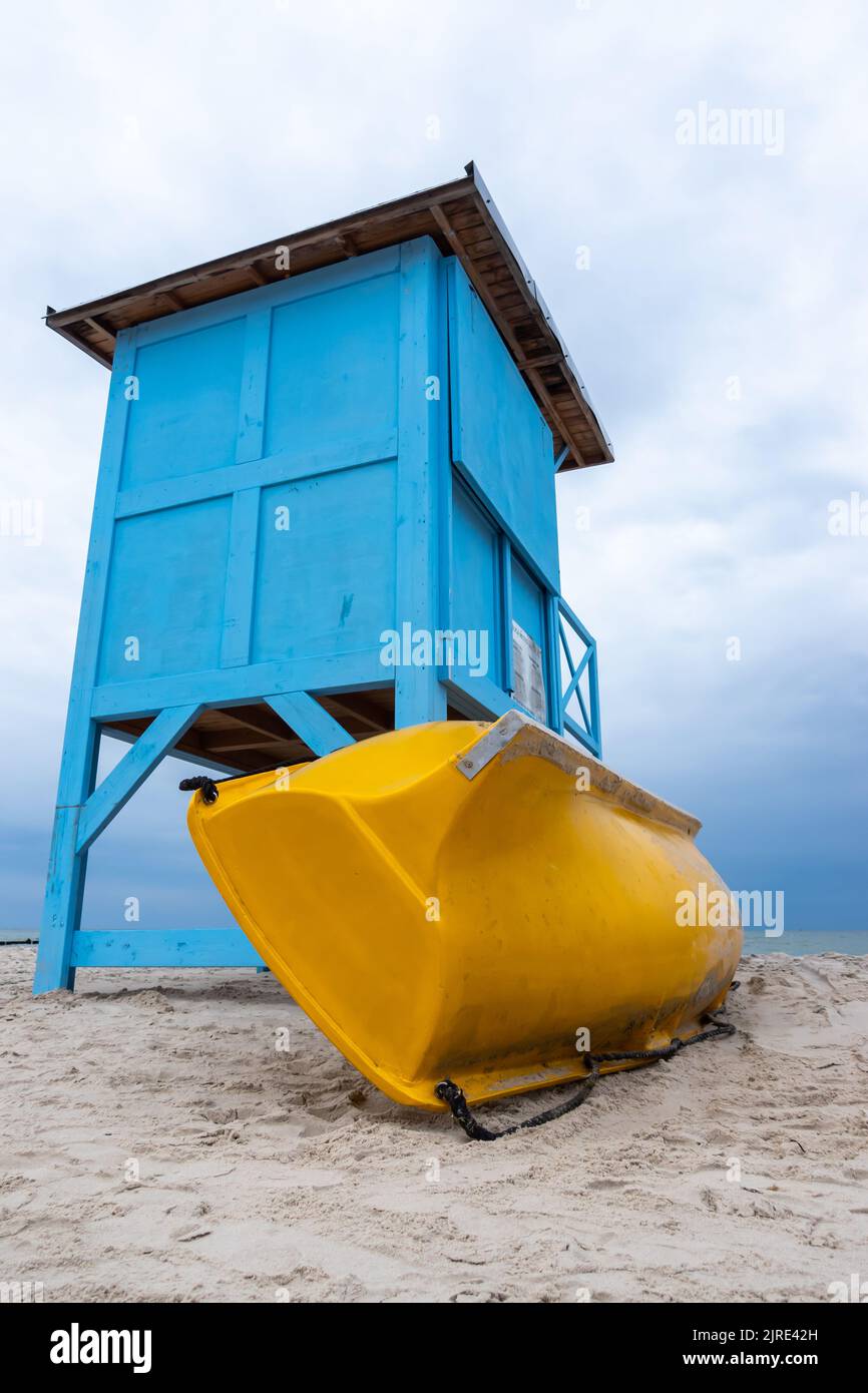 A blue lifeguard booth on the beach on a cloudy day. A yellow lifeboat ...