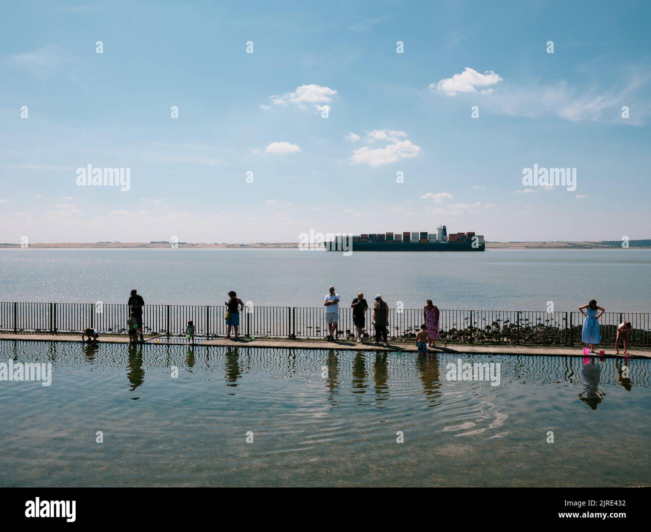 A large cargo freight container ship passes the tidal lido and summer ...