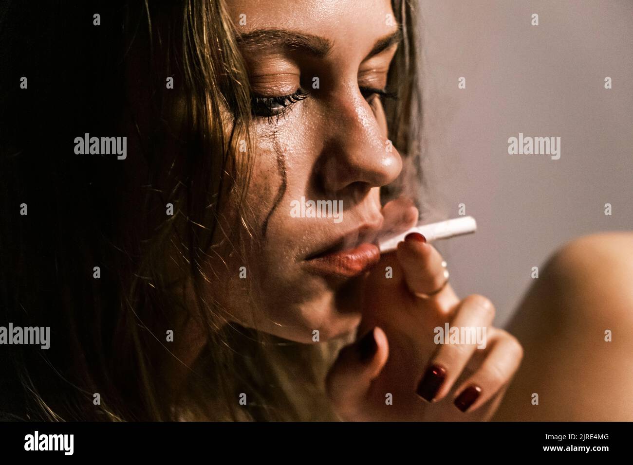 Crying young woman with cigarette in her mouth. Portrait of side view ...