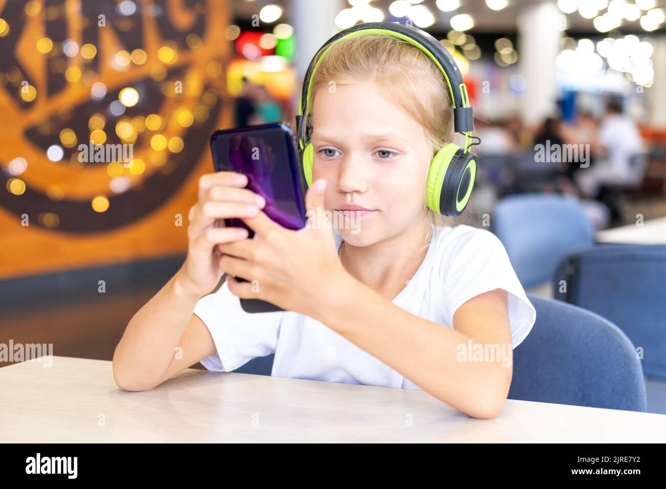 A little girl with headphones is watching cartoons on her phone sitting ...