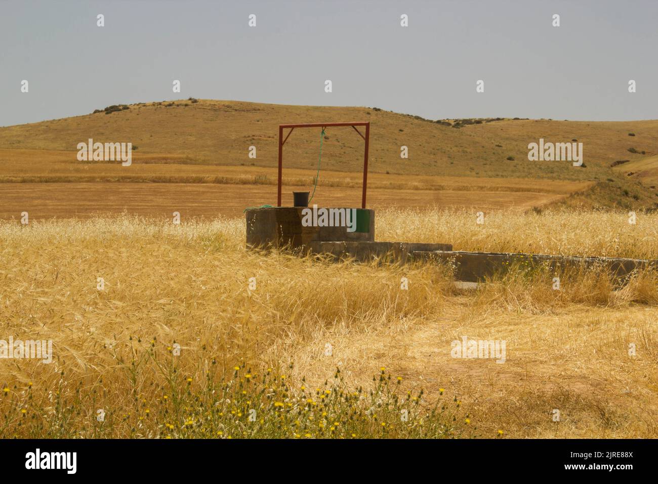 A scenic view of a well with a basket in a field of dried grass against ...