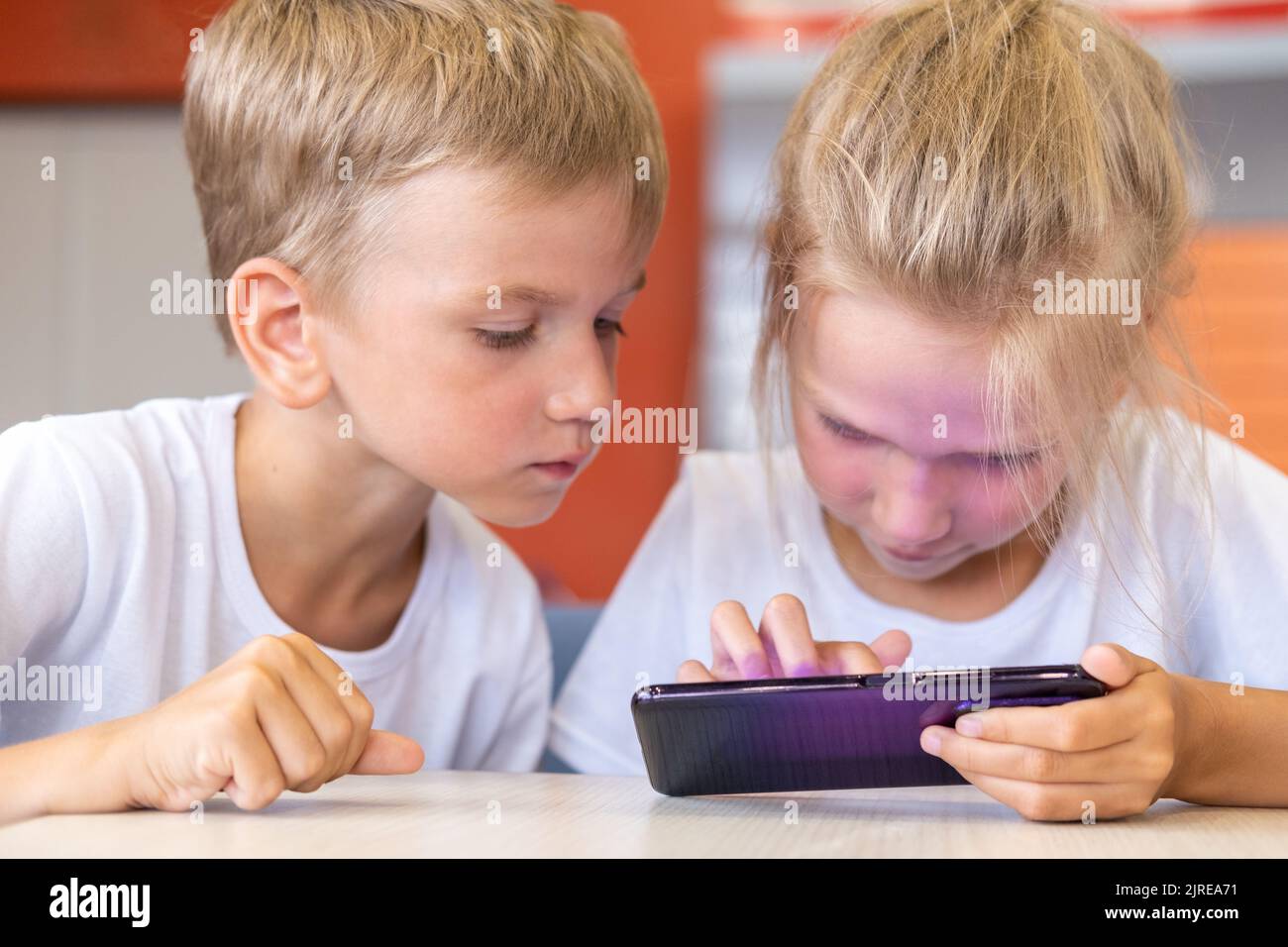 A little girl and a boy are watching cartoons on their phone, sitting ...