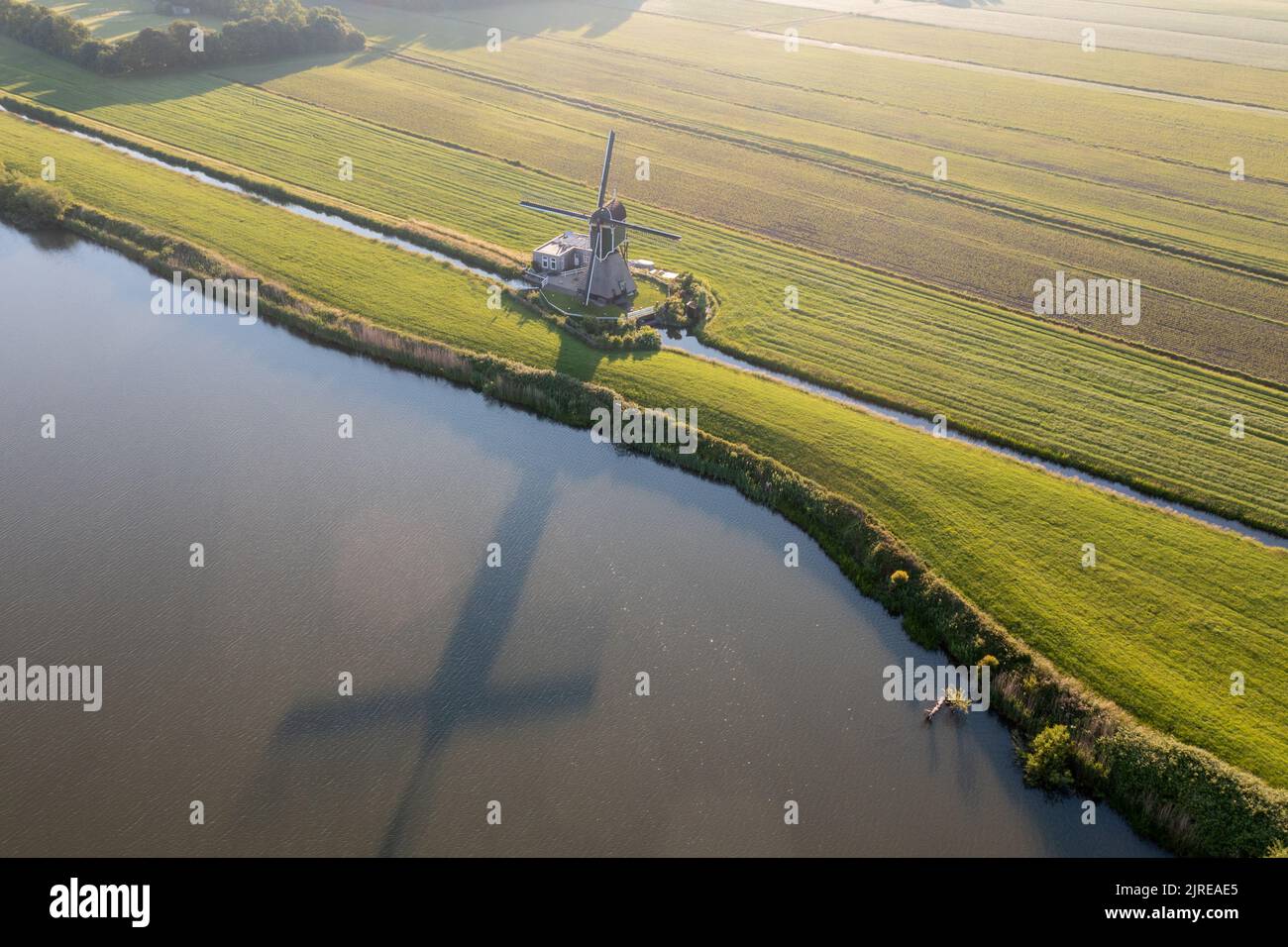 An aerial shot of a seesaw windmill by the river, early in the morning ...