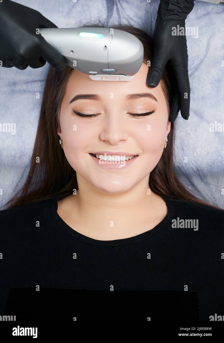 Top view of beautiful young woman with closed eyes having face lifting procedure and smiling ...