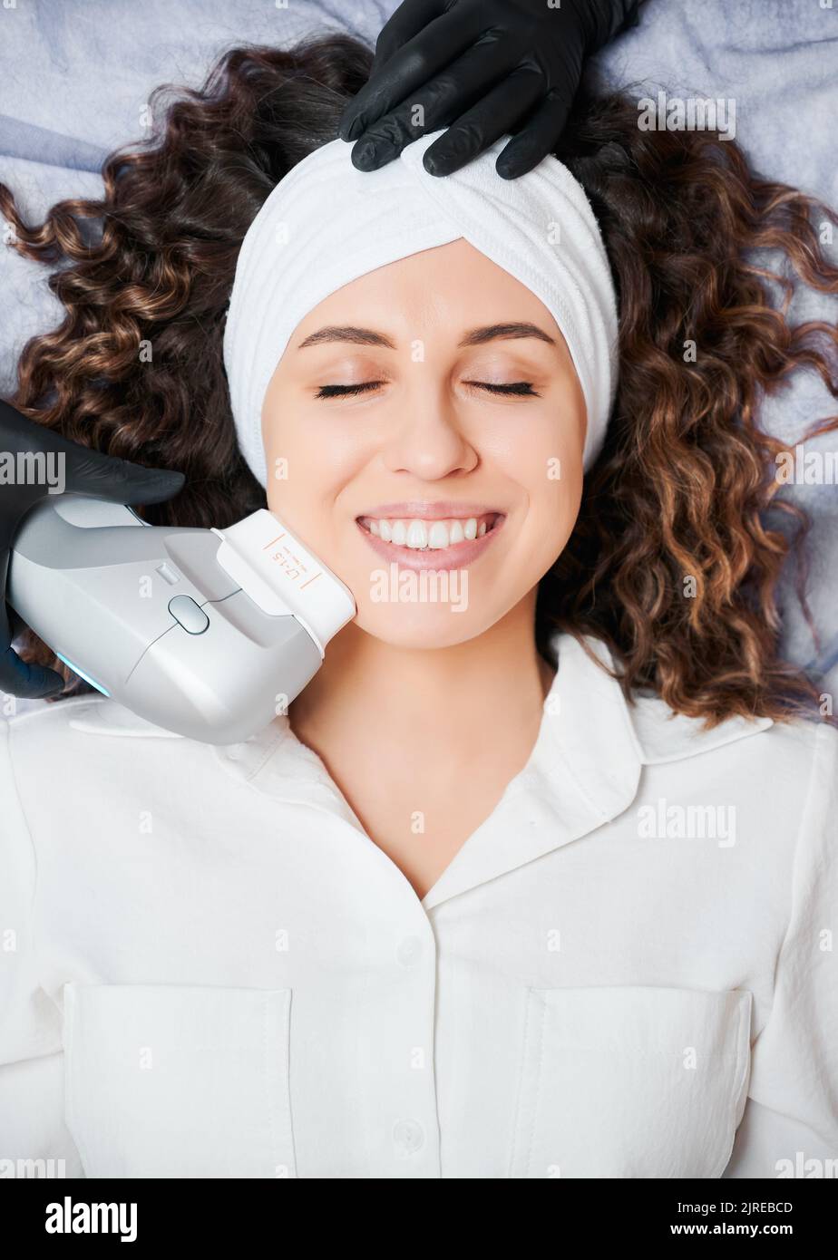 Top view of beautiful young woman with closed eyes wearing white headband while receiving facial ...