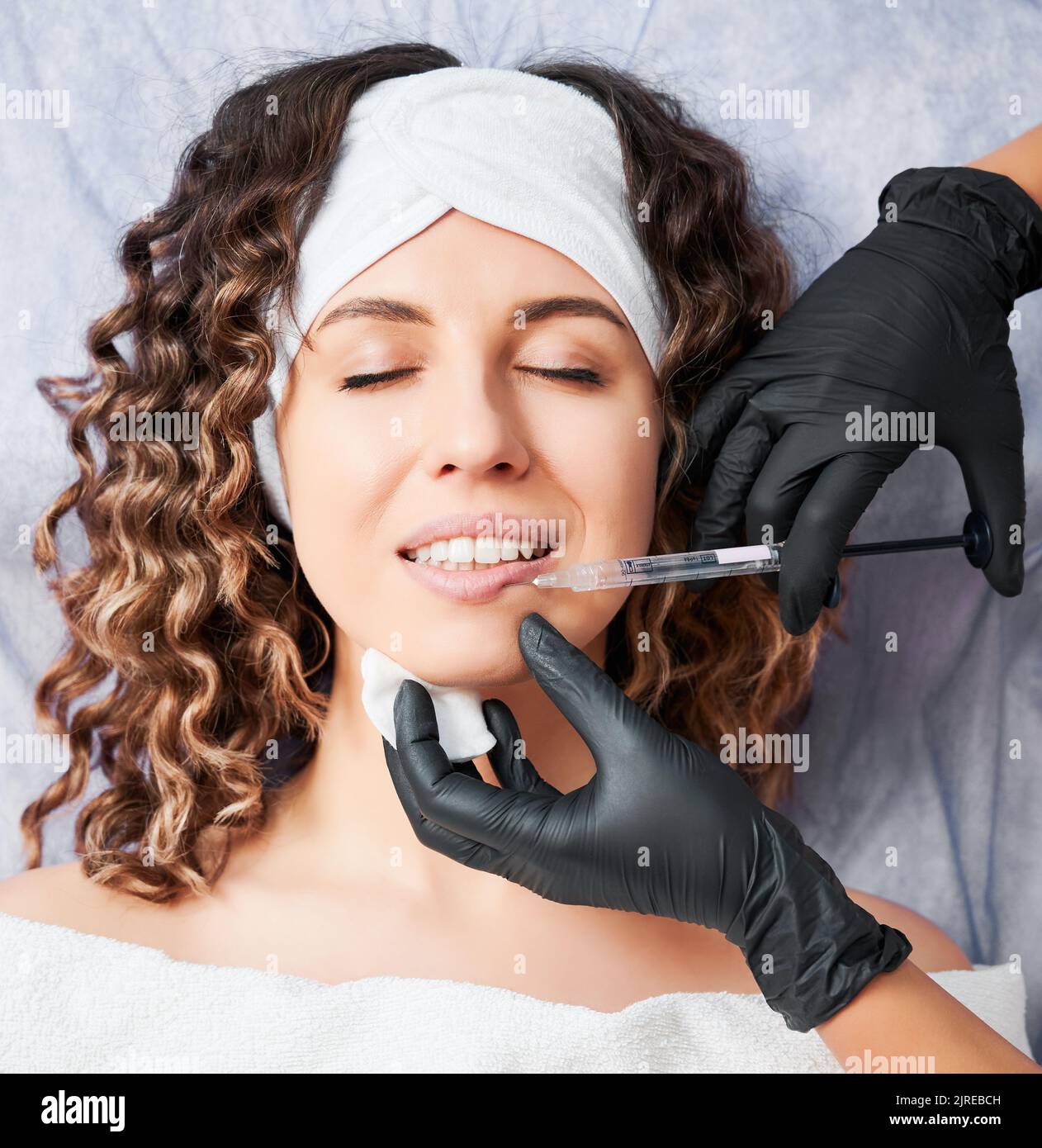 Close up of doctor cosmetologist hands in sterile gloves making injection in woman lips. Smiling ...