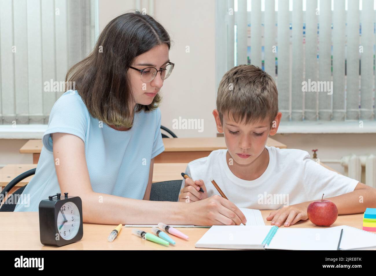 A boy and a teacher doing homework, writing text in a notebook at the ...