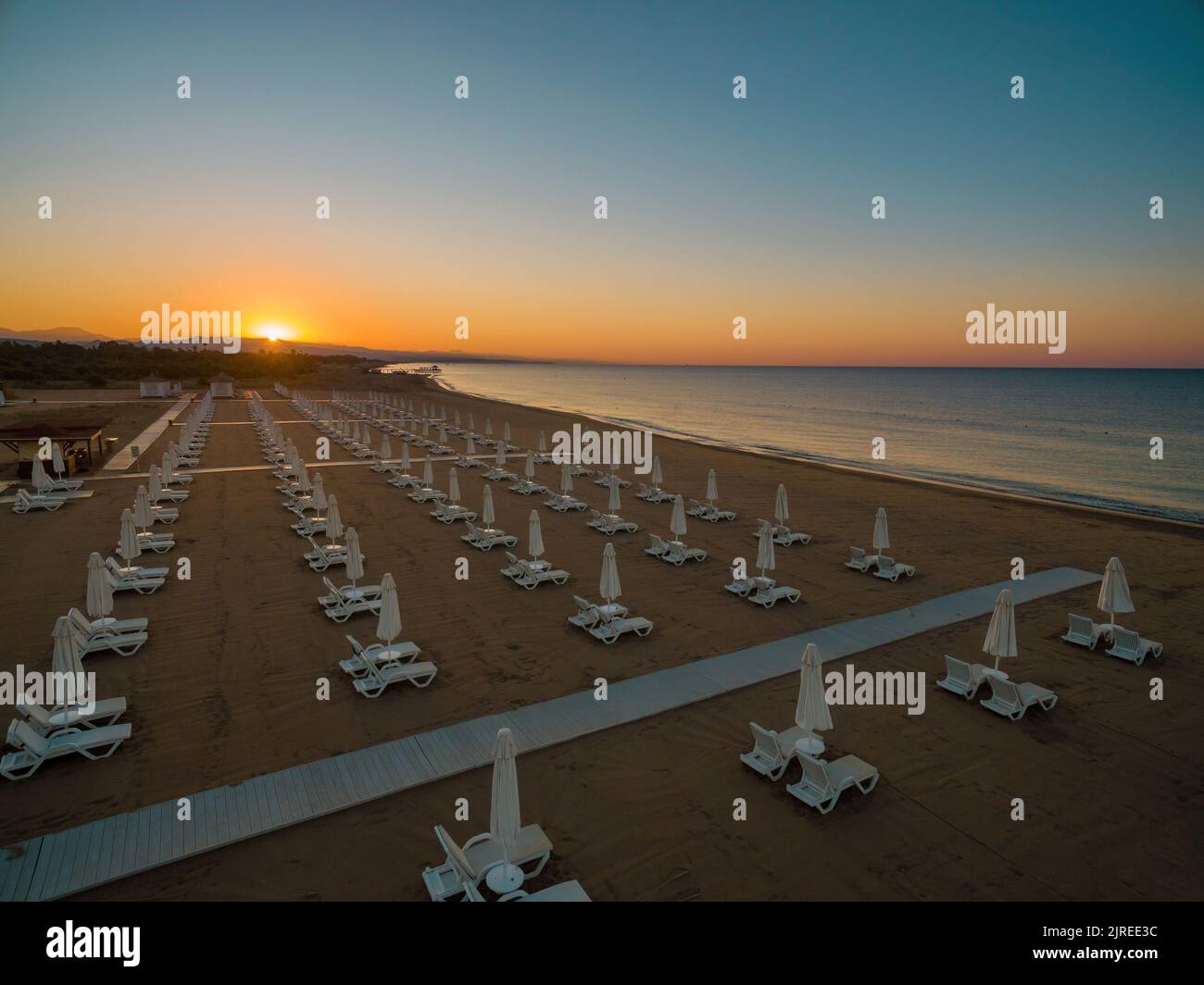 Aerial view of parasols and sun loungers on calm sea beach at sunrise ...