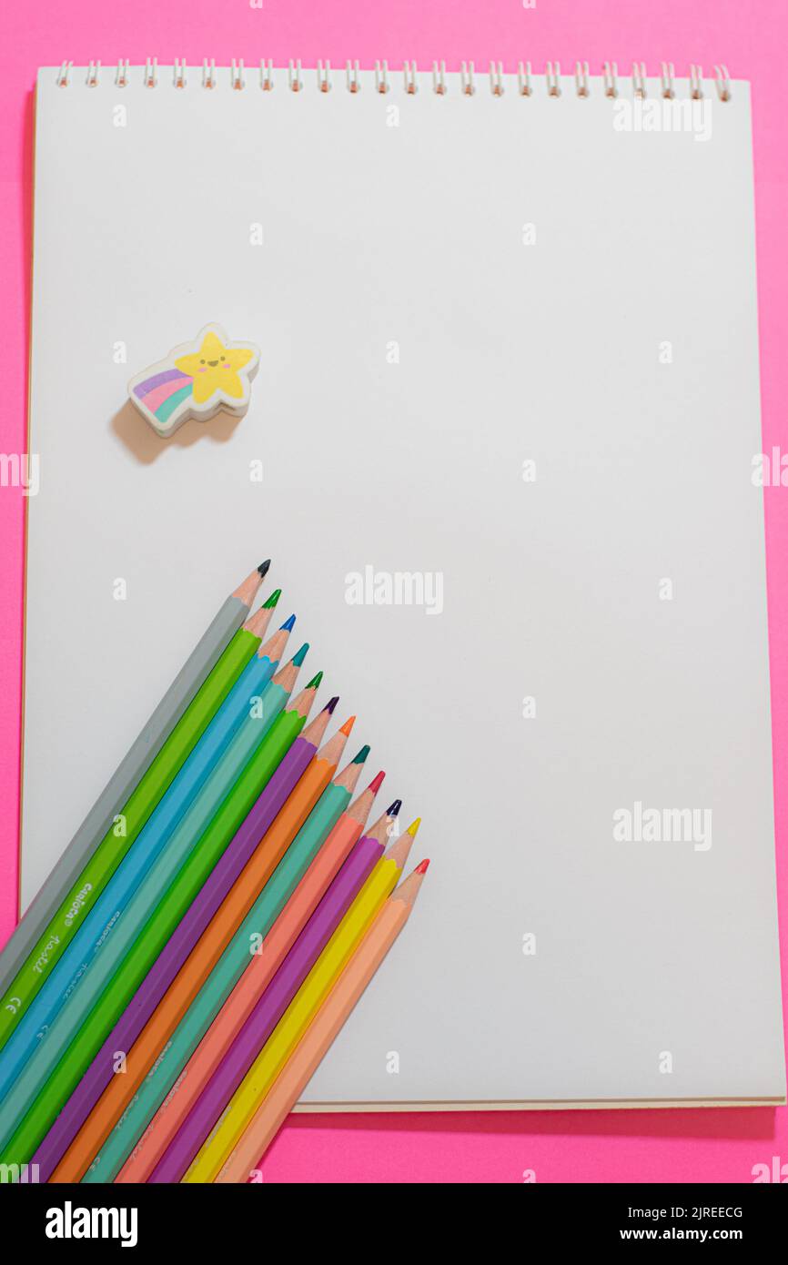 Top view of colored pencils and drawing pads on pink background. Blank ...