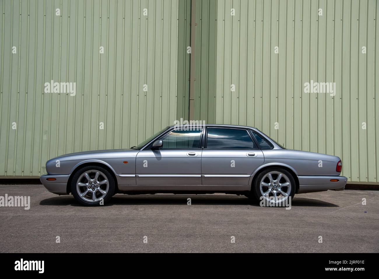 Silver Jaguar XJR (X308) parked in from of a high corrugated steel wall ...