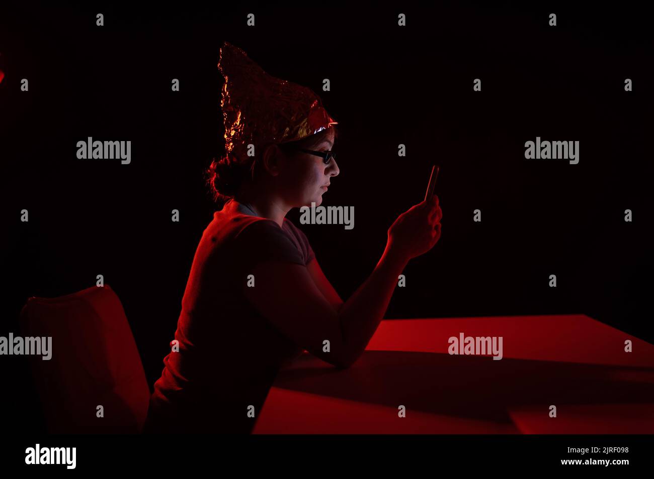 Paranoid caucasian woman using smartphone wearing tinfoil hat ...