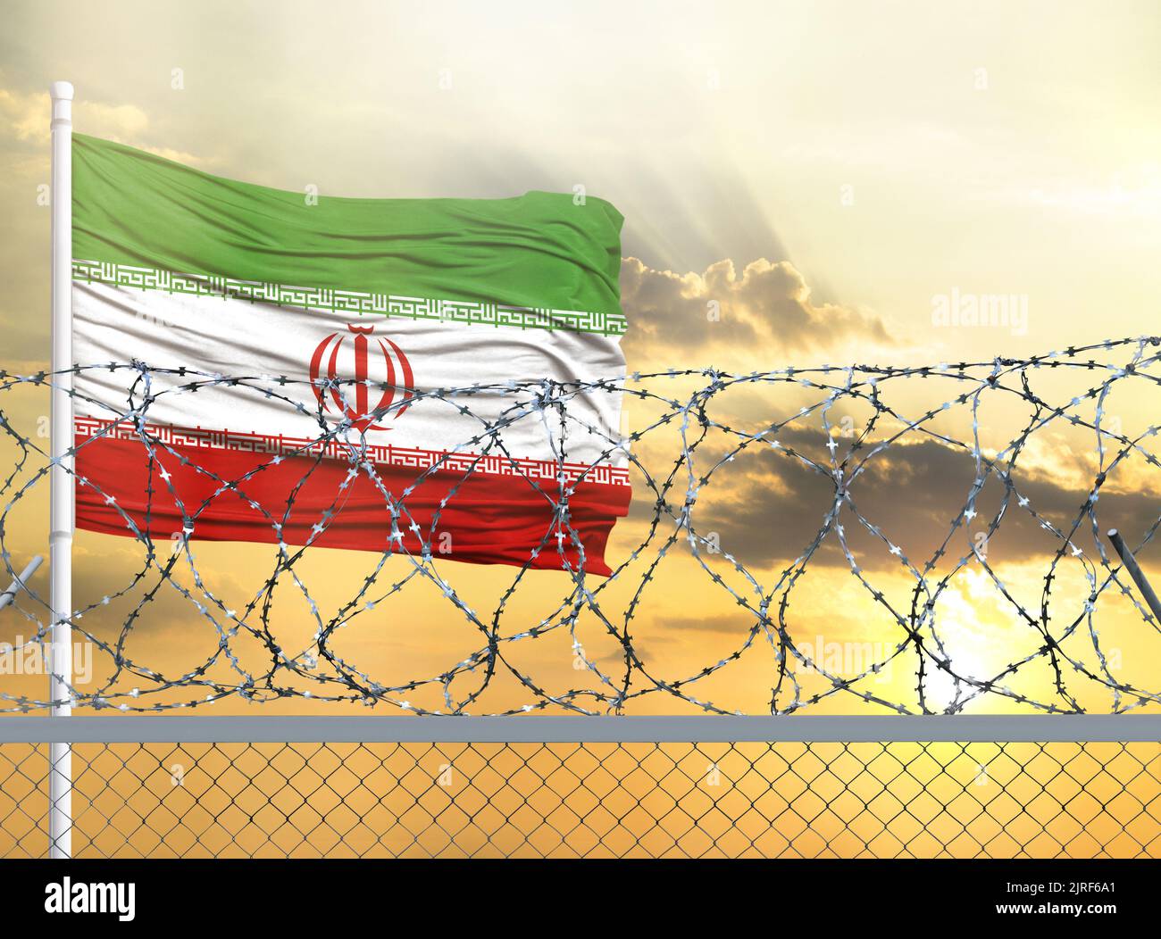 Flagpole with the flag of Iran against the sky and behind a fence with ...