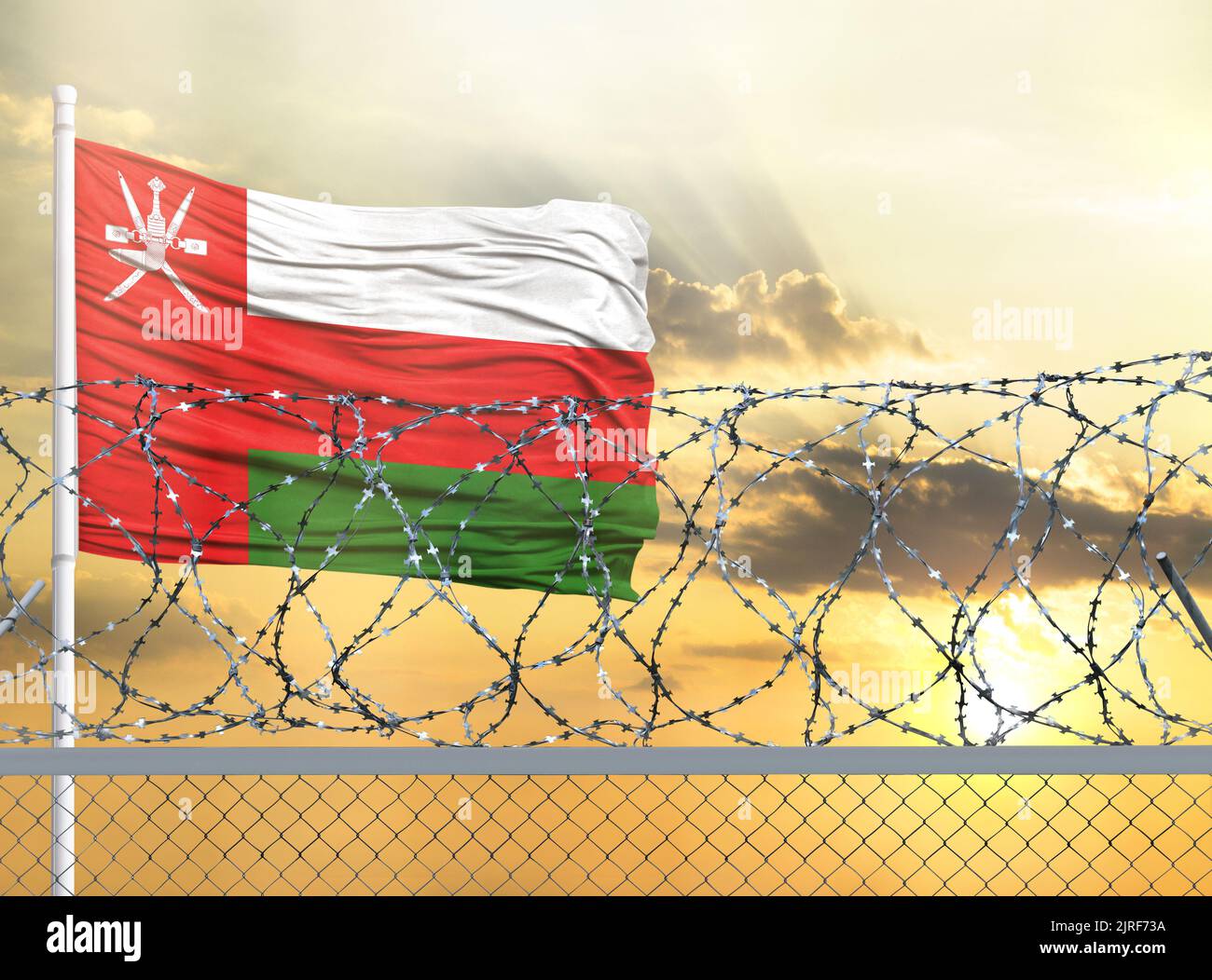 Flagpole with the flag of Oman against the sky and behind a fence with ...
