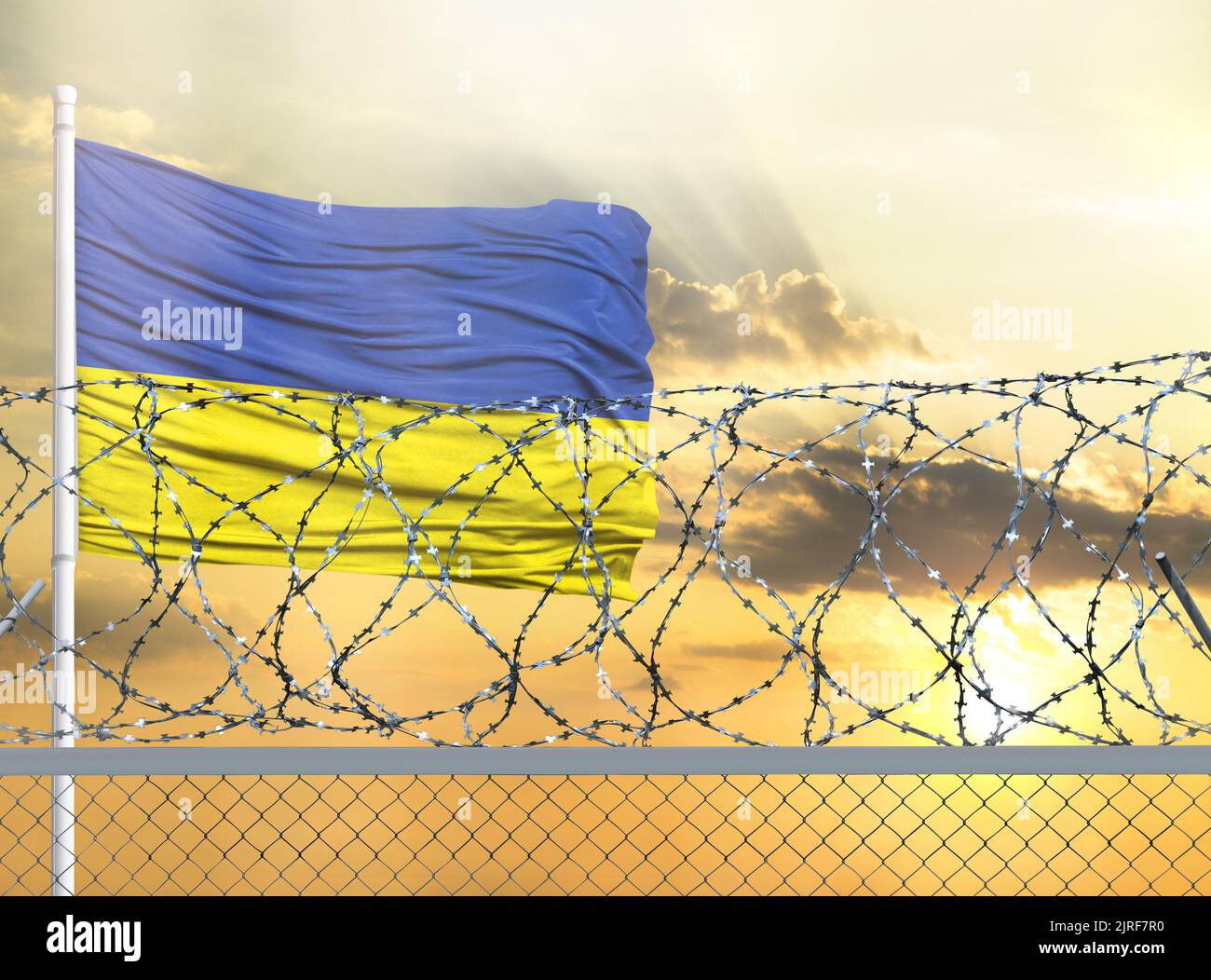 Flagpole with the flag of Ukraine against the sky and behind a fence ...