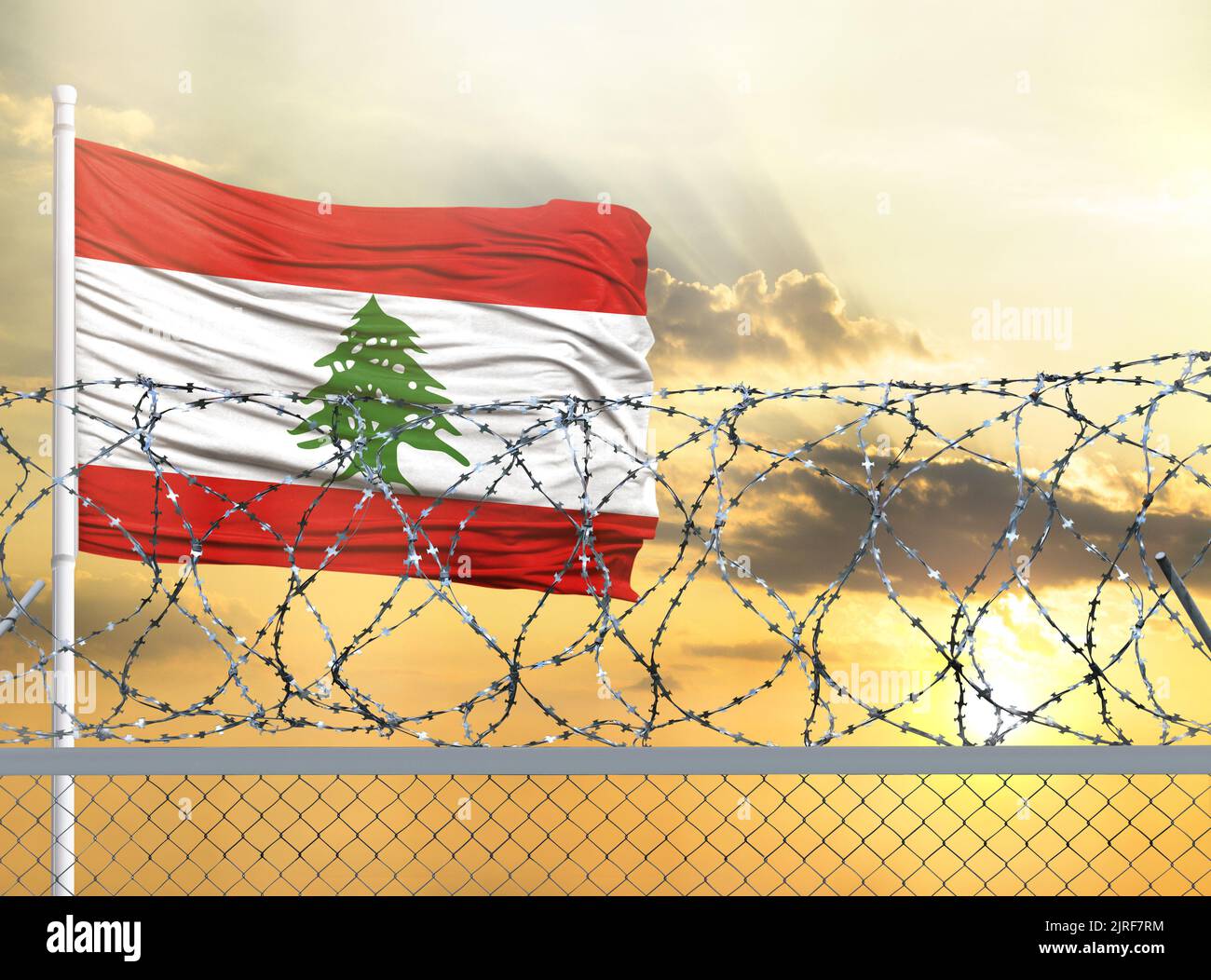 Flagpole with the flag of Lebanon against the sky and behind a fence ...