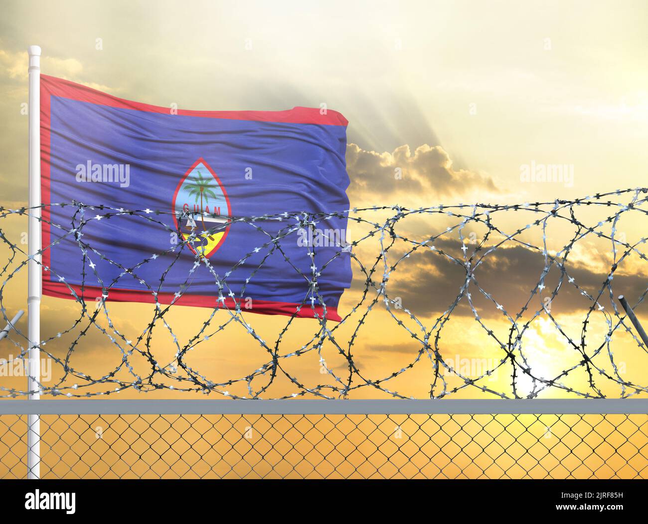 Flagpole with the flag of Guam against the sky and behind a fence with ...