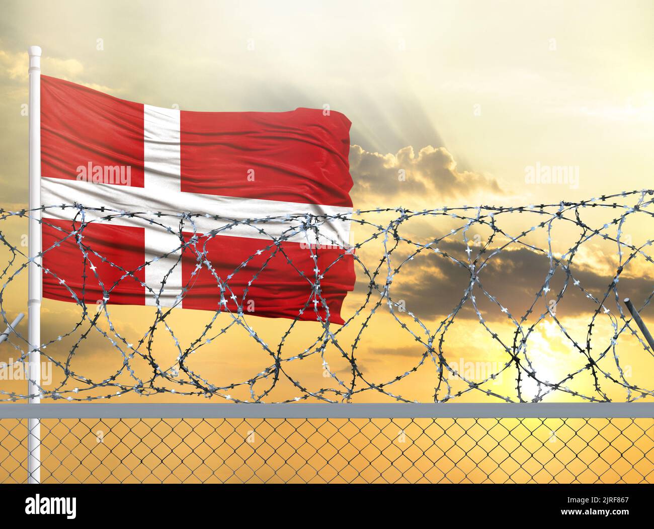 Flagpole with the flag of Denmark against the sky and behind a fence ...
