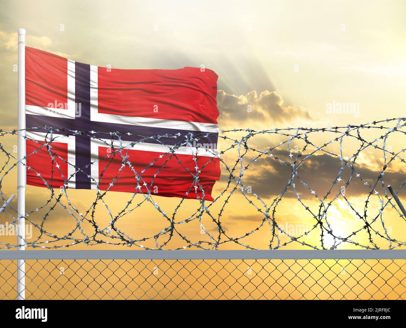 Flagpole with the flag of Norway against the sky and behind a fence ...