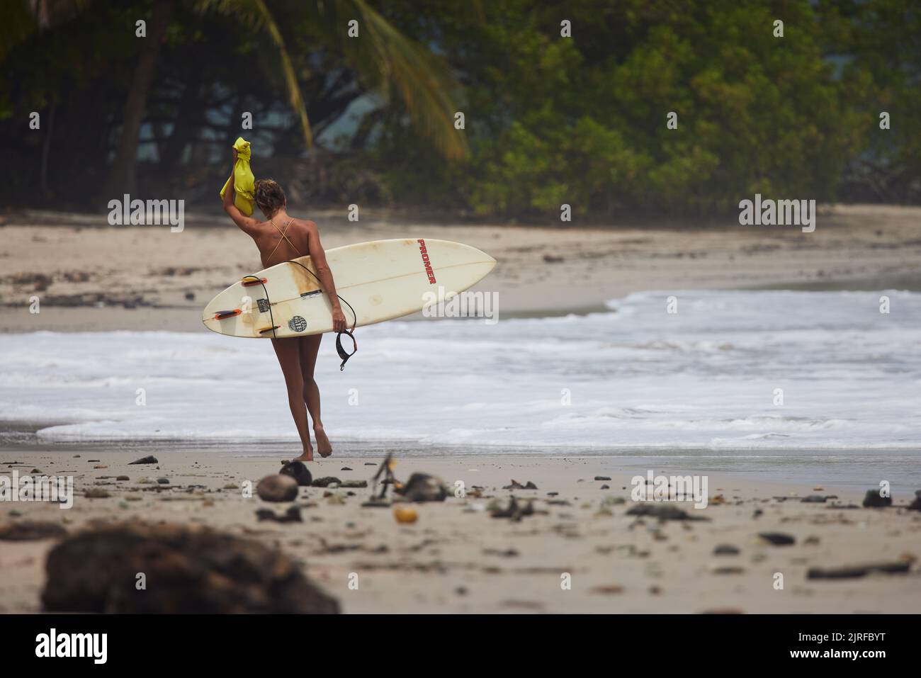 A back view of surfer holding surfboard and walking on sandy beach ...