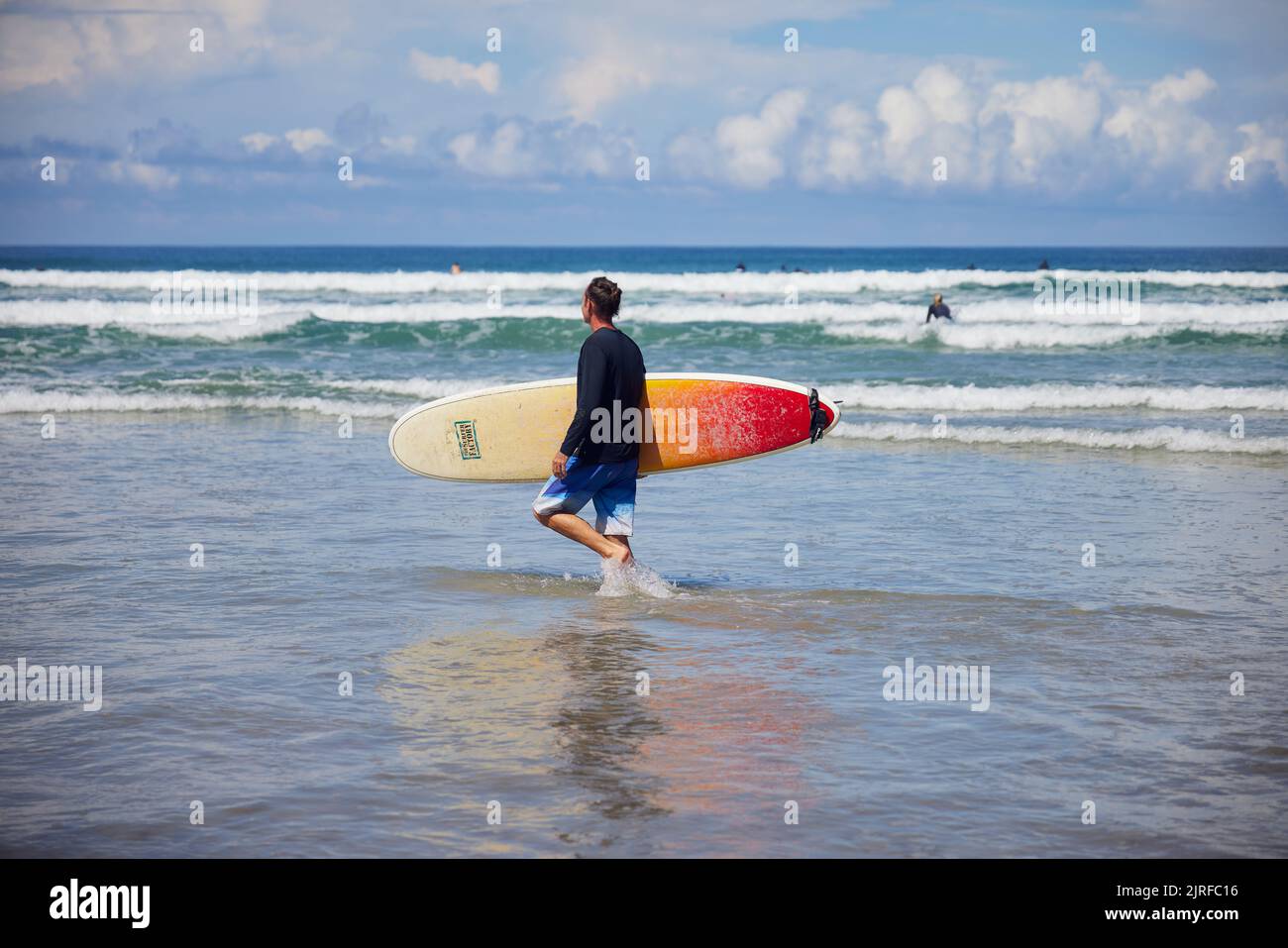 A side view of surfer holding surfboard and walking in water Stock ...