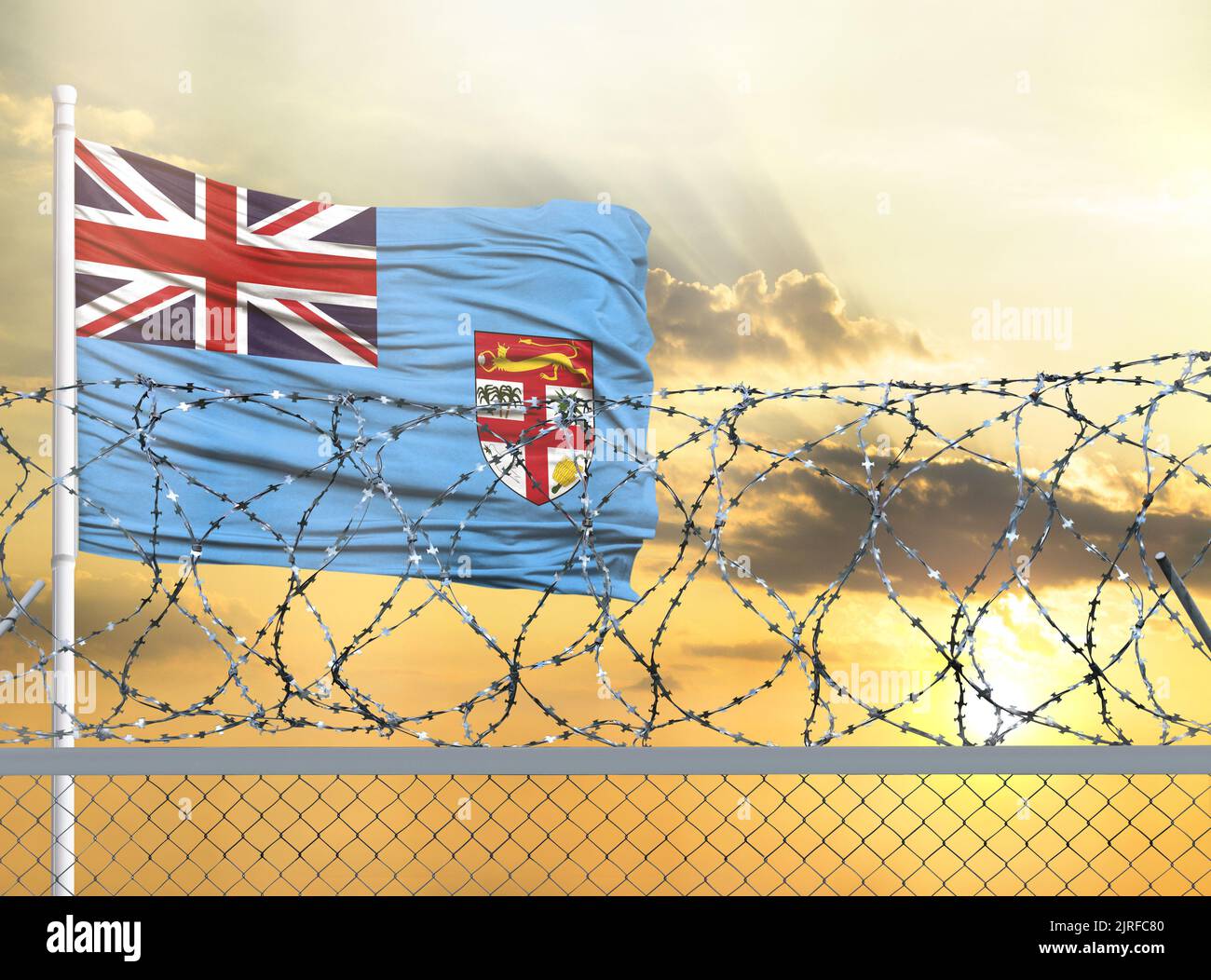 Flagpole with the flag of Fiji against the sky and behind a fence with ...