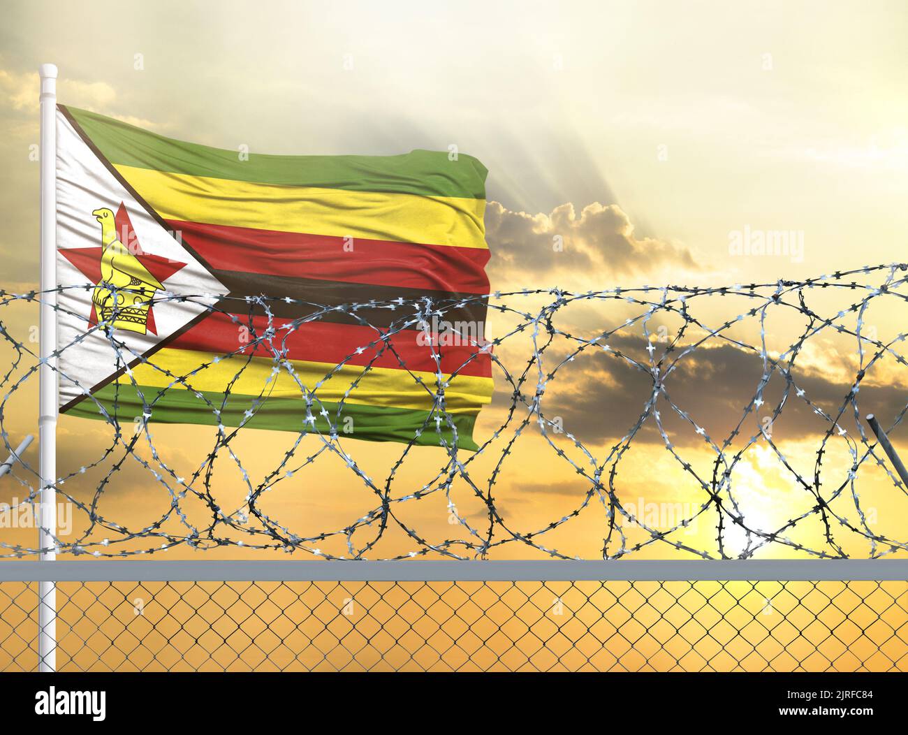 Flagpole with the flag of Zimbabwe against the sky and behind a fence ...