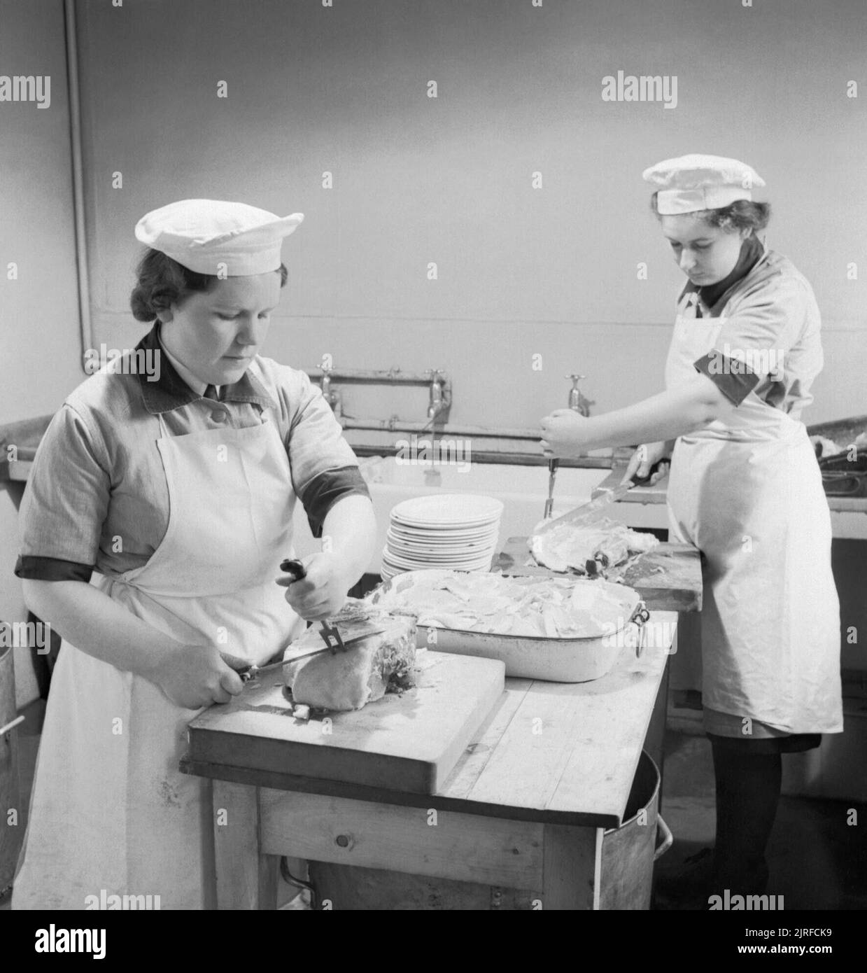 Two Wren cooks carve ham for the lunchtime meal in the galley of a ...