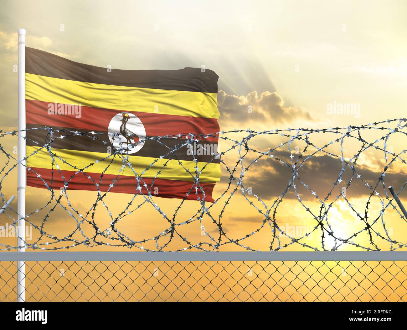 Flagpole with the flag of Uganda against the sky and behind a fence ...