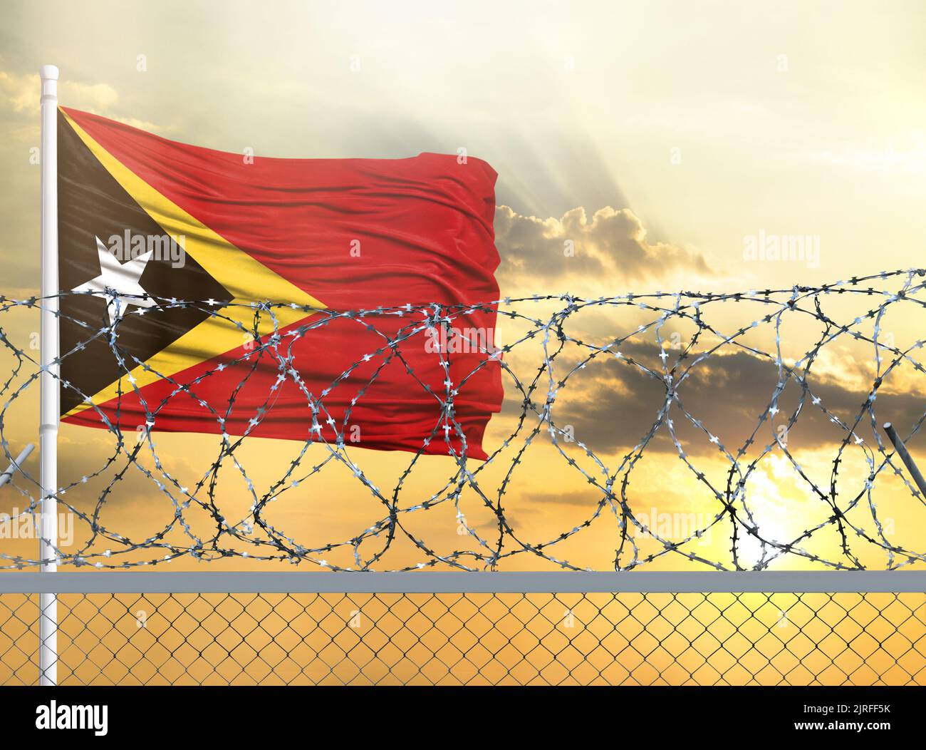 Flagpole with the flag of East Timor against the sky and behind a fence ...