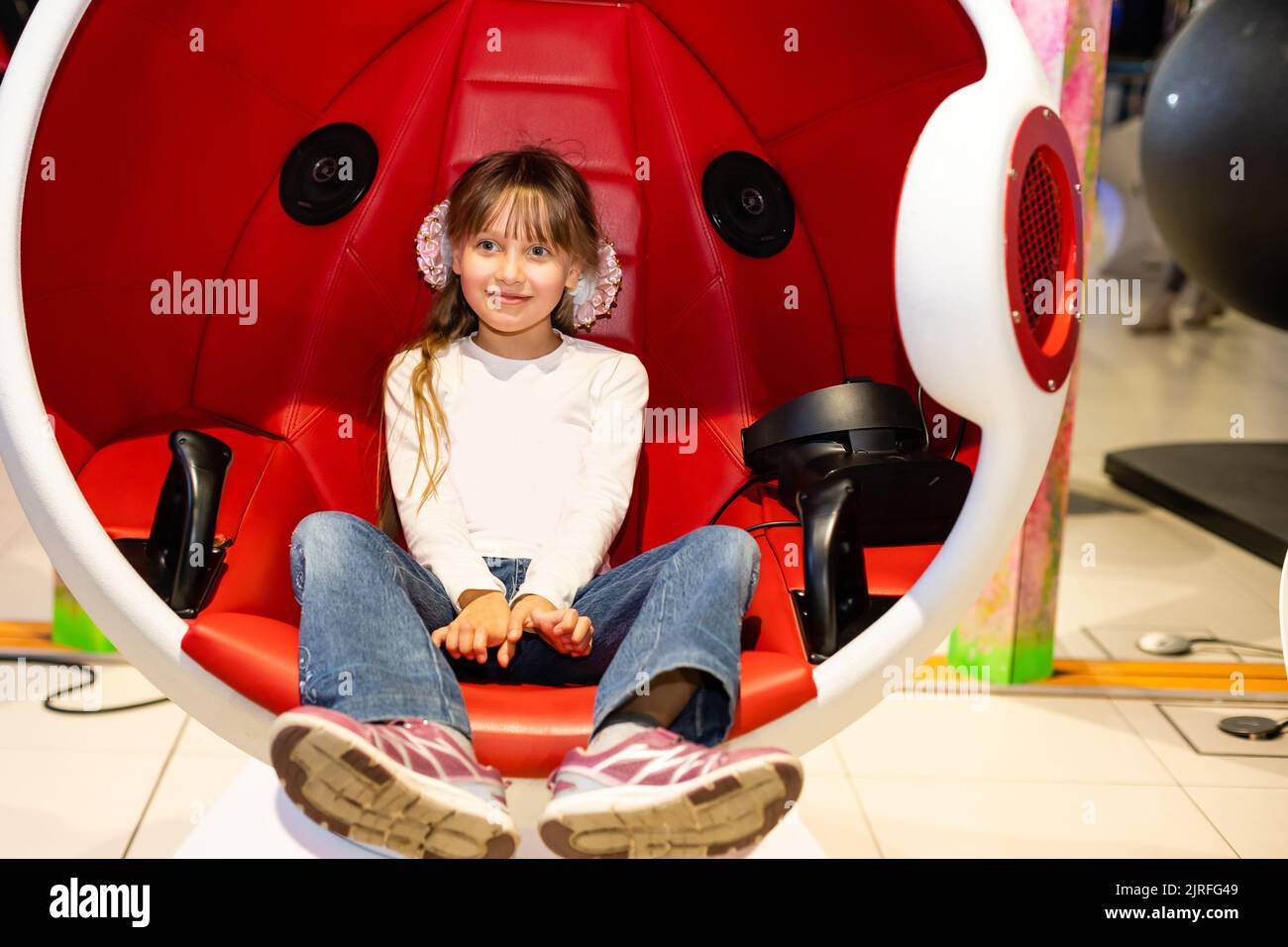 A little girl sitting in a gaming cockpit and holding the race steering ...