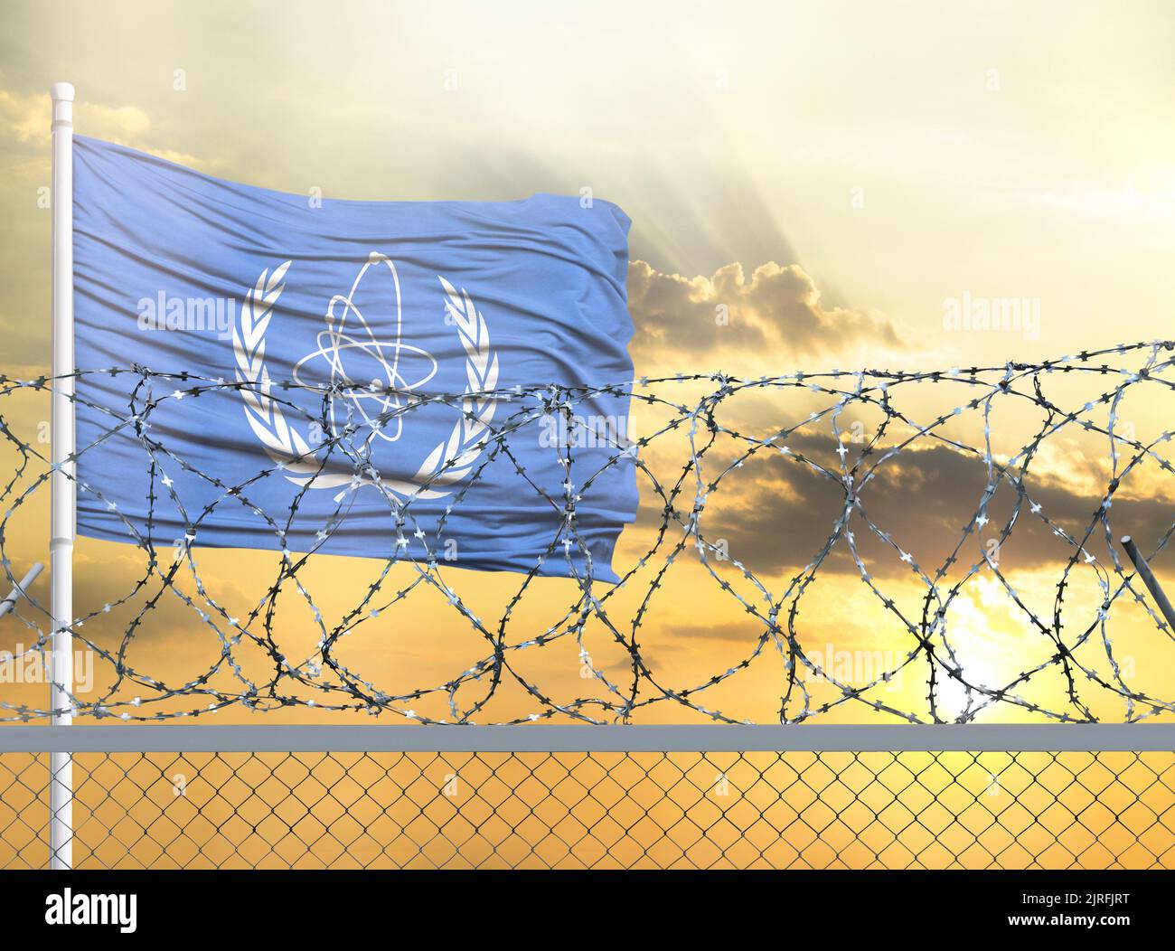 Flagpole with the flag of IAEA against the sky and behind a fence with ...