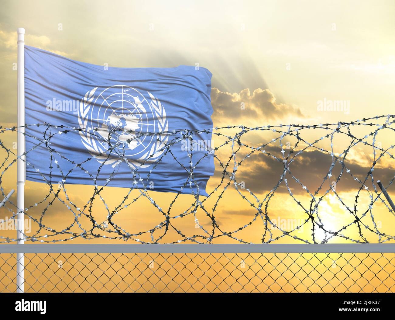 Flagpole with the flag of UN against the sky and behind a fence with ...