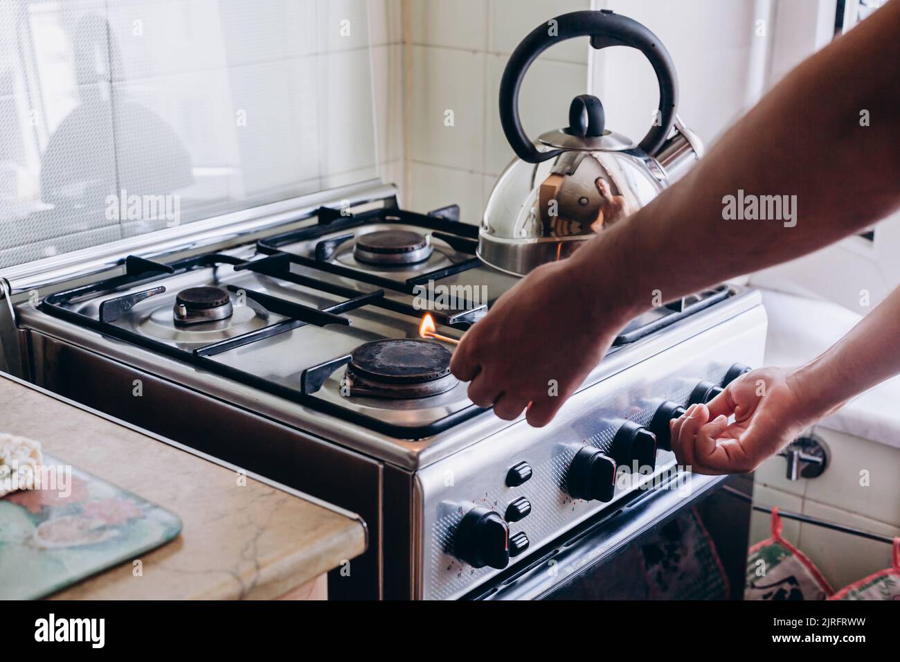 A man's hand with a match lights a gas burner or a gas stove in the ...