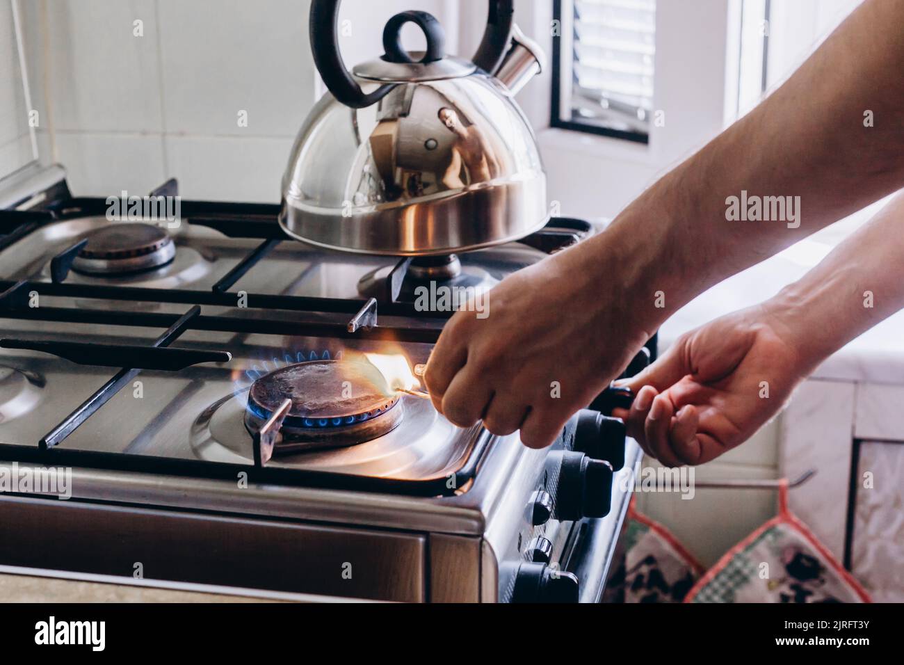A man's hand with a match lights a gas burner or a gas stove in the ...