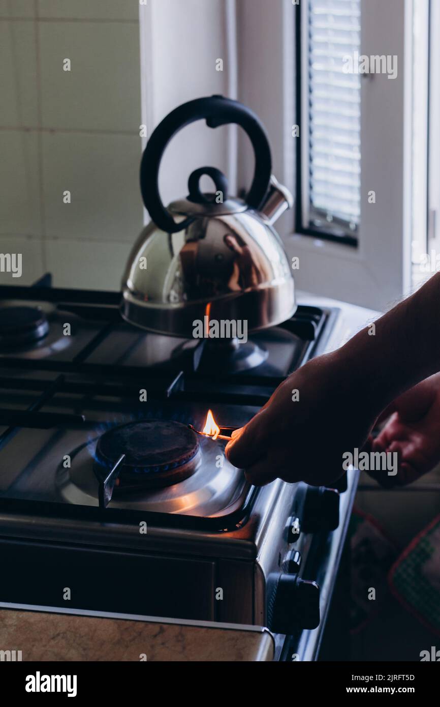 A man's hand with a match lights a gas burner or a gas stove in the ...