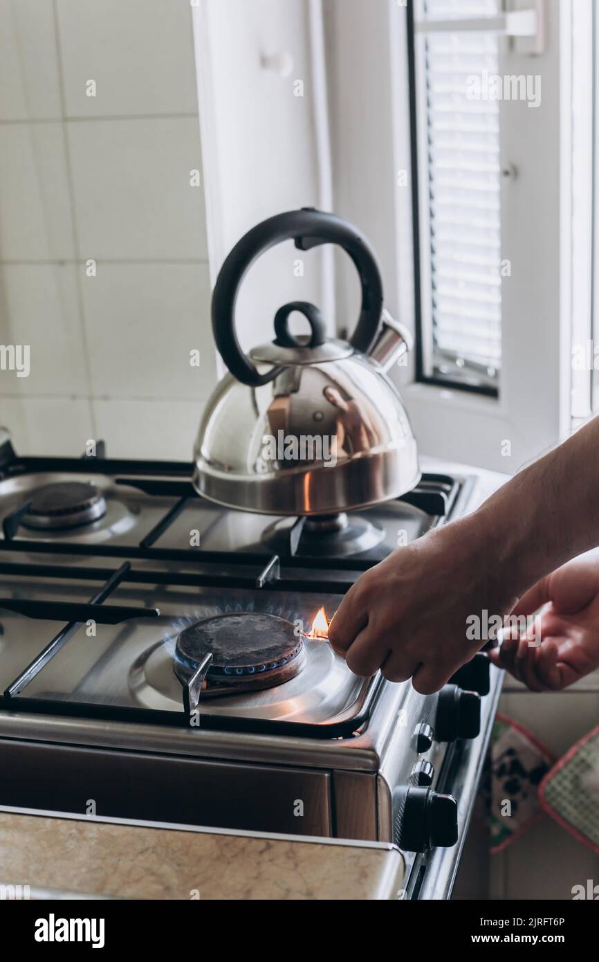 A man's hand with a match lights a gas burner or a gas stove in the ...