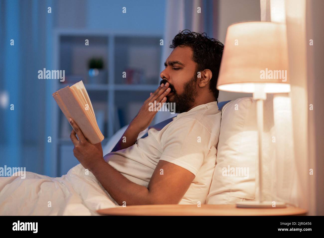 yawning indian man reading book in bed at night Stock Photo - Alamy