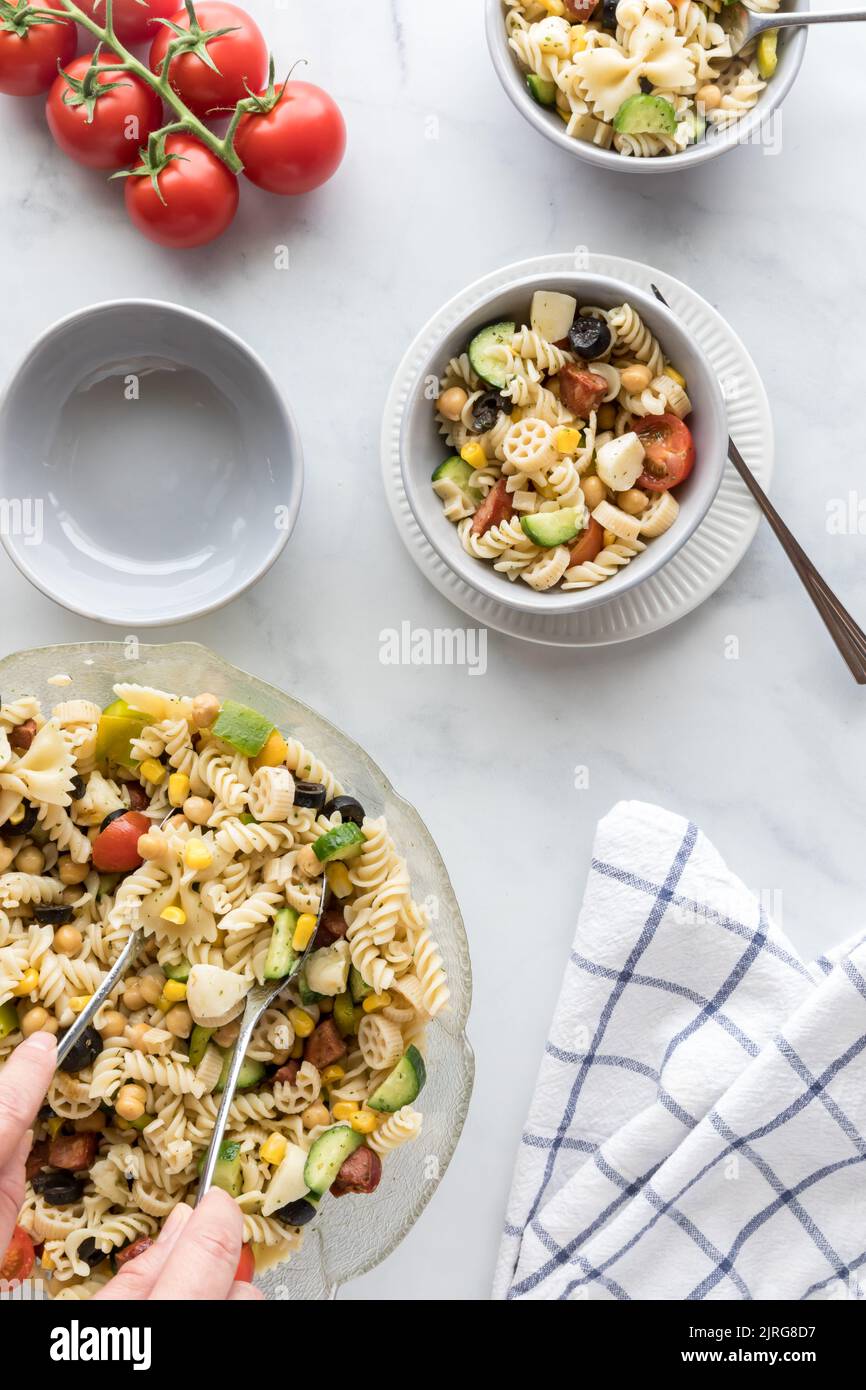 Hands holding serving utensils to serve up bowls of fresh homemade pasta salad Stock Photo - Alamy